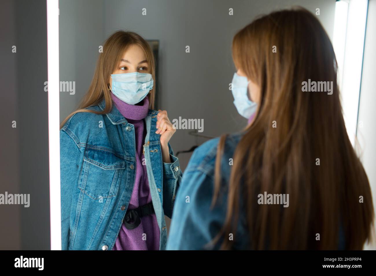 Young woman in face mask try on clothes in dressing room with mirror in ...