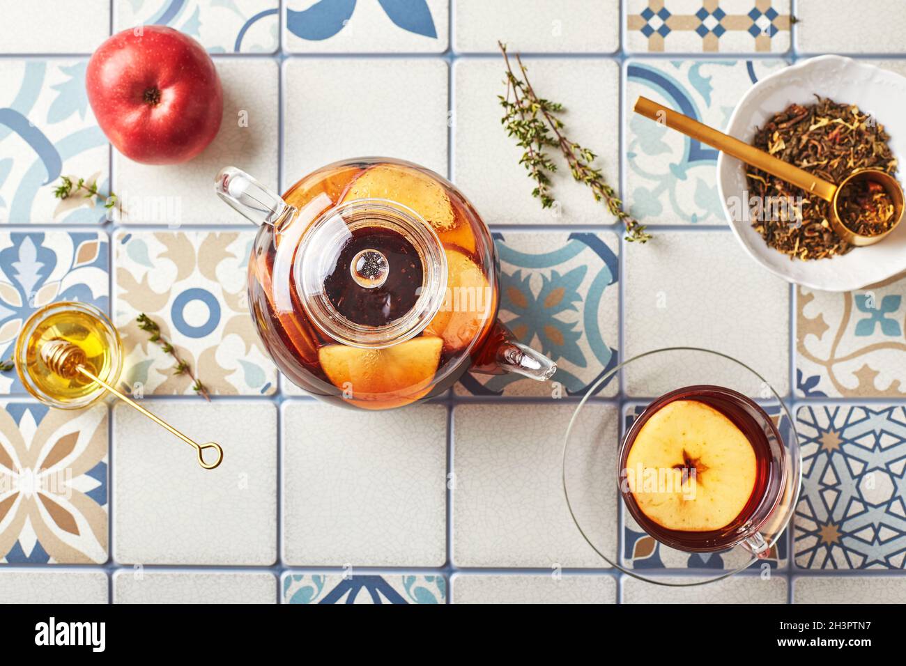 Fruit tea with apples and thyme in glass teapot and cup on table made ...