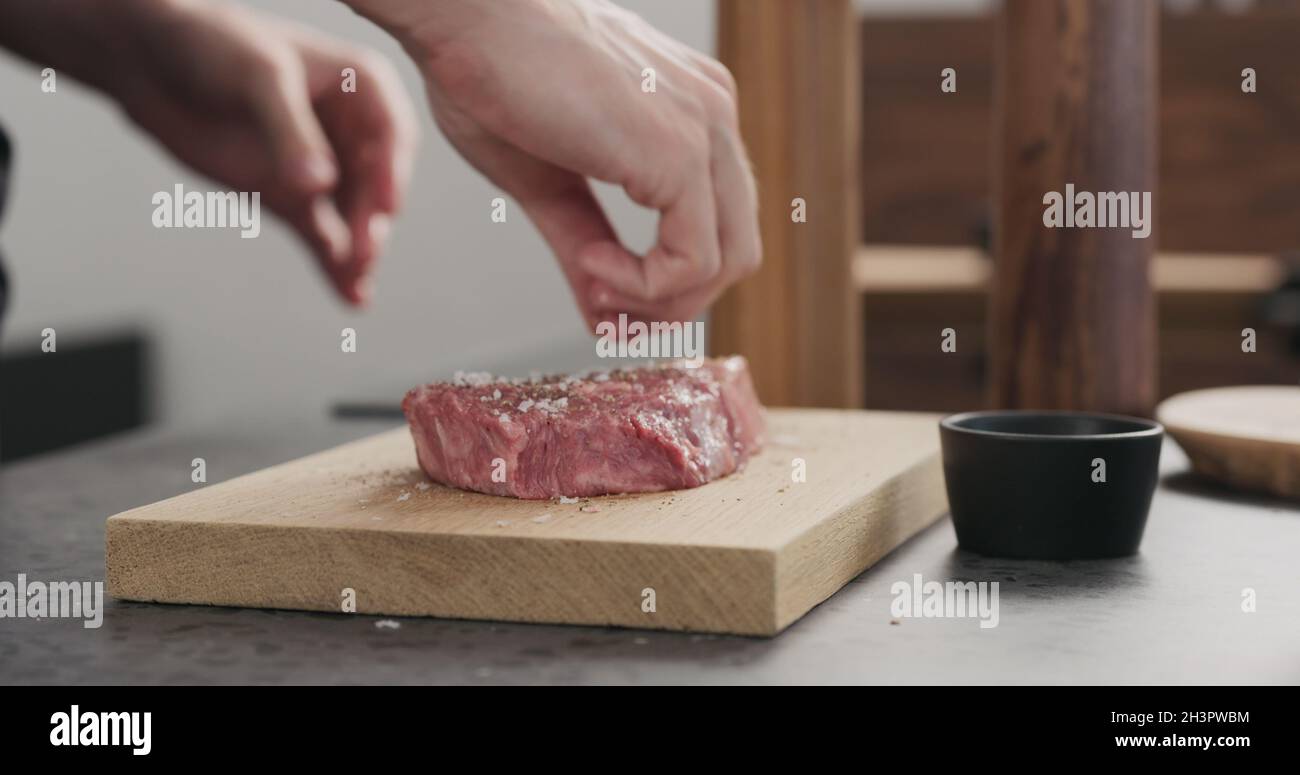 Man seasoning raw ribeye steak on oak wood board, wide photo Stock ...