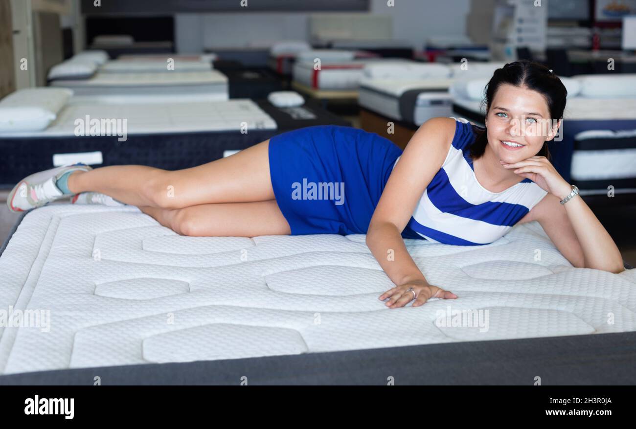 Customer girl is posing lying on new mattress before buying it in shop ...