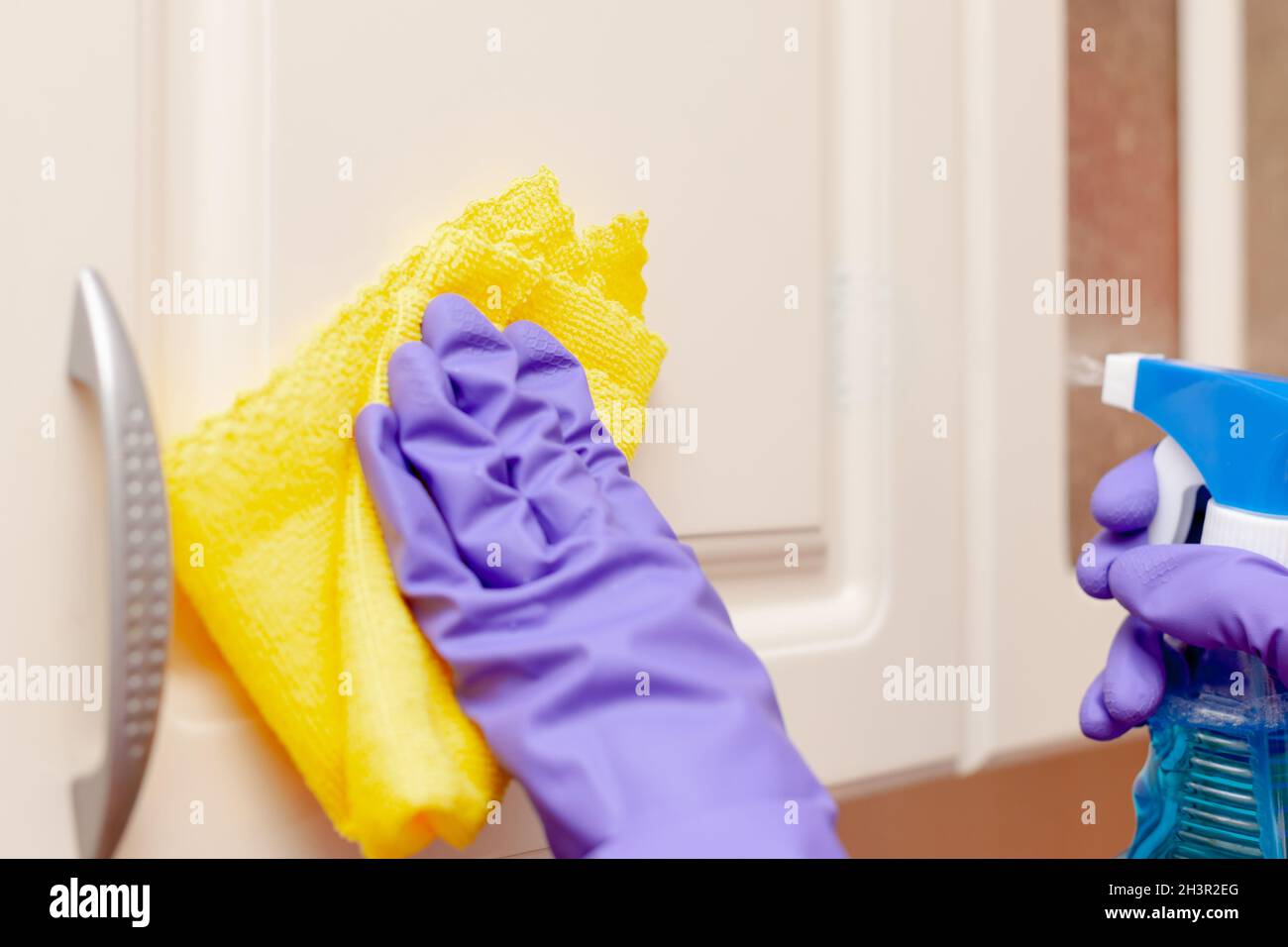 female hand in a purple rubber glove wipes the beige kitchen cabinet ...