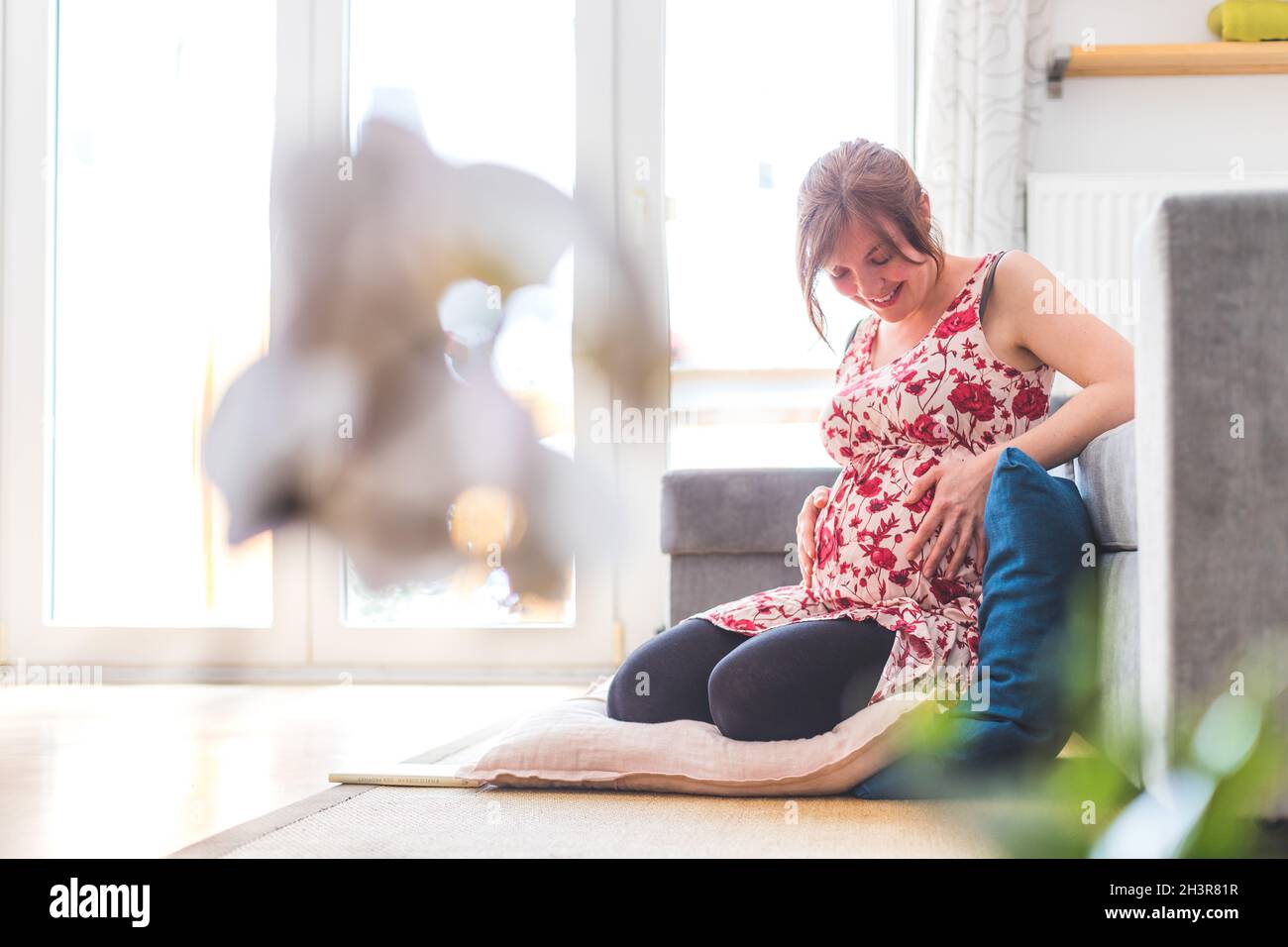 Happy pregnant mother is sitting on the floor, hugging her tummy Stock ...