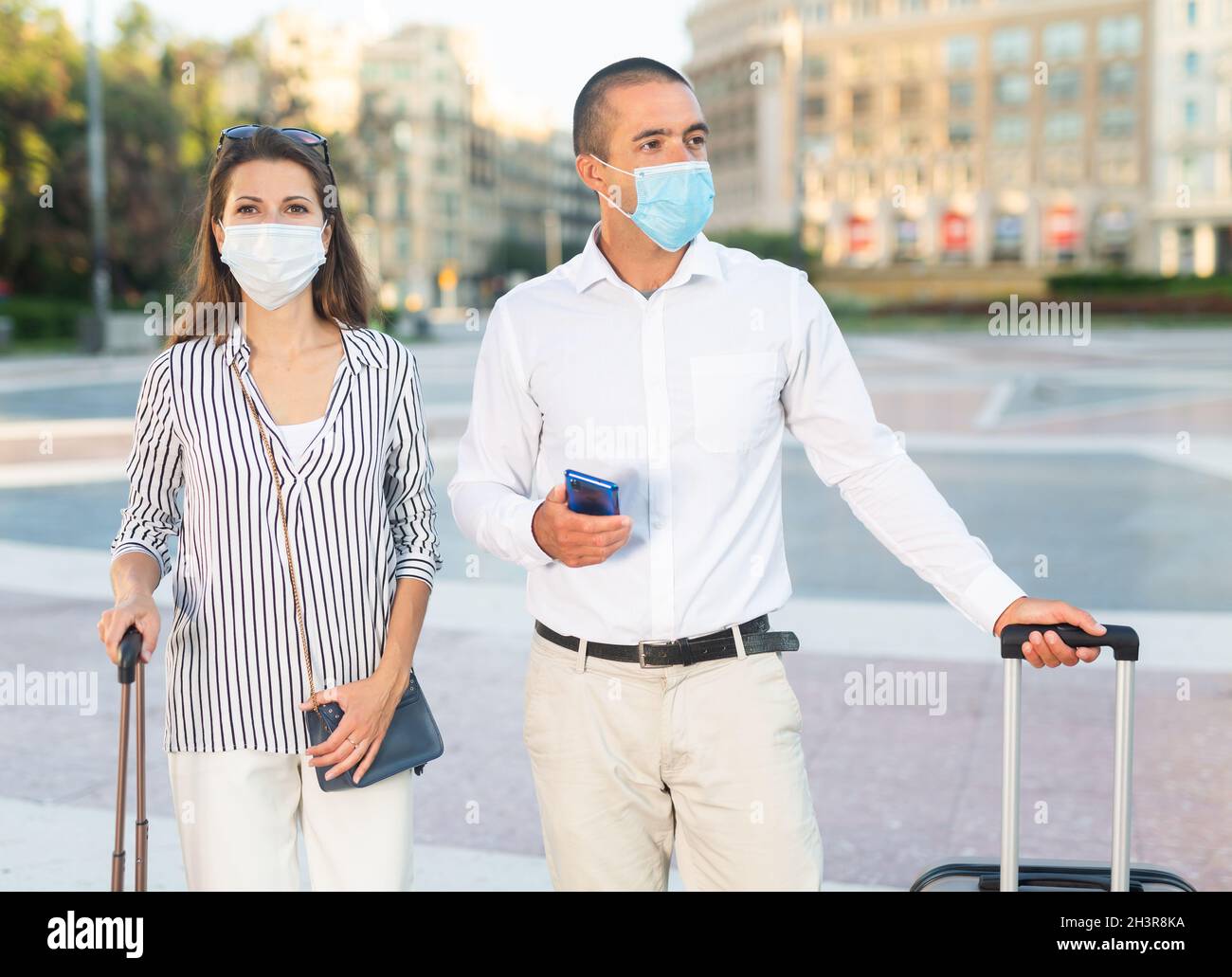Tourist couple in face masks walking with suitcases Stock Photo - Alamy