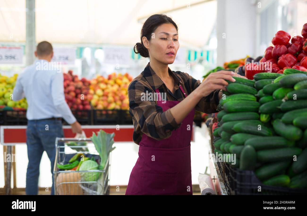 Supermarket worker putting cucumber on counter Stock Photo - Alamy