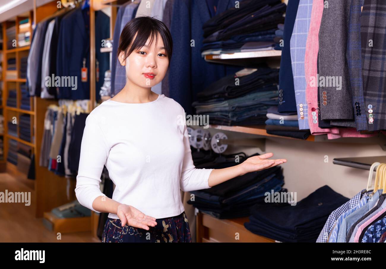 Chinese female shopping assistant offering various shirt in men cloths ...