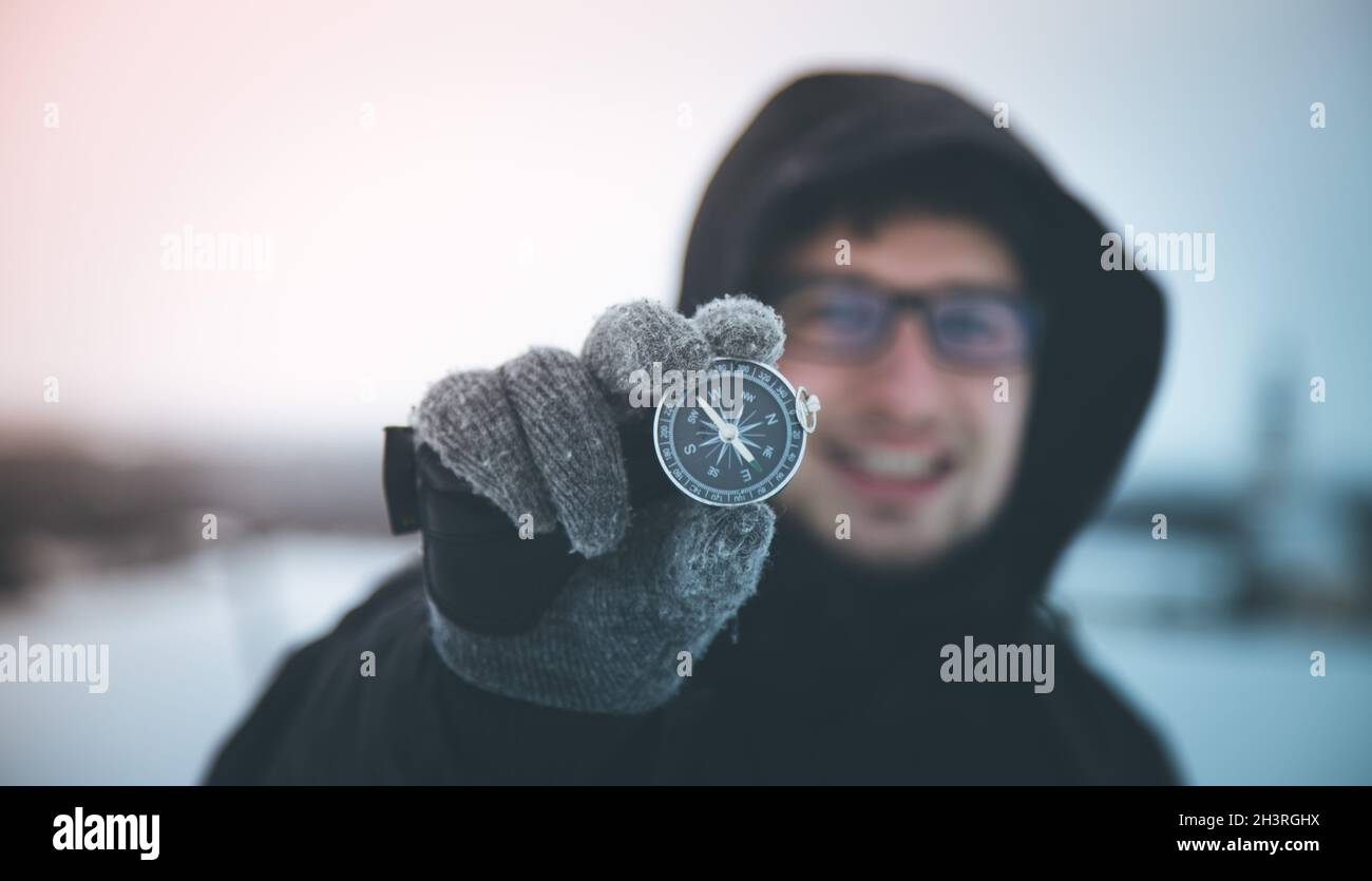 Young man with gloves is holding up a compass, outside in the winter ...