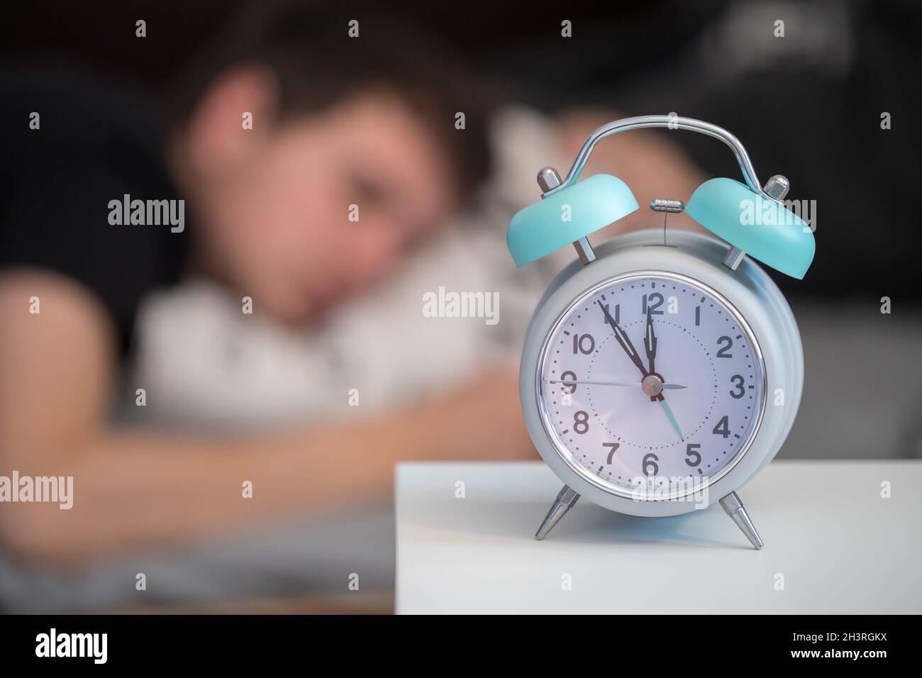 Alarm clock in the morning. Young man sleeps in the blurry background ...