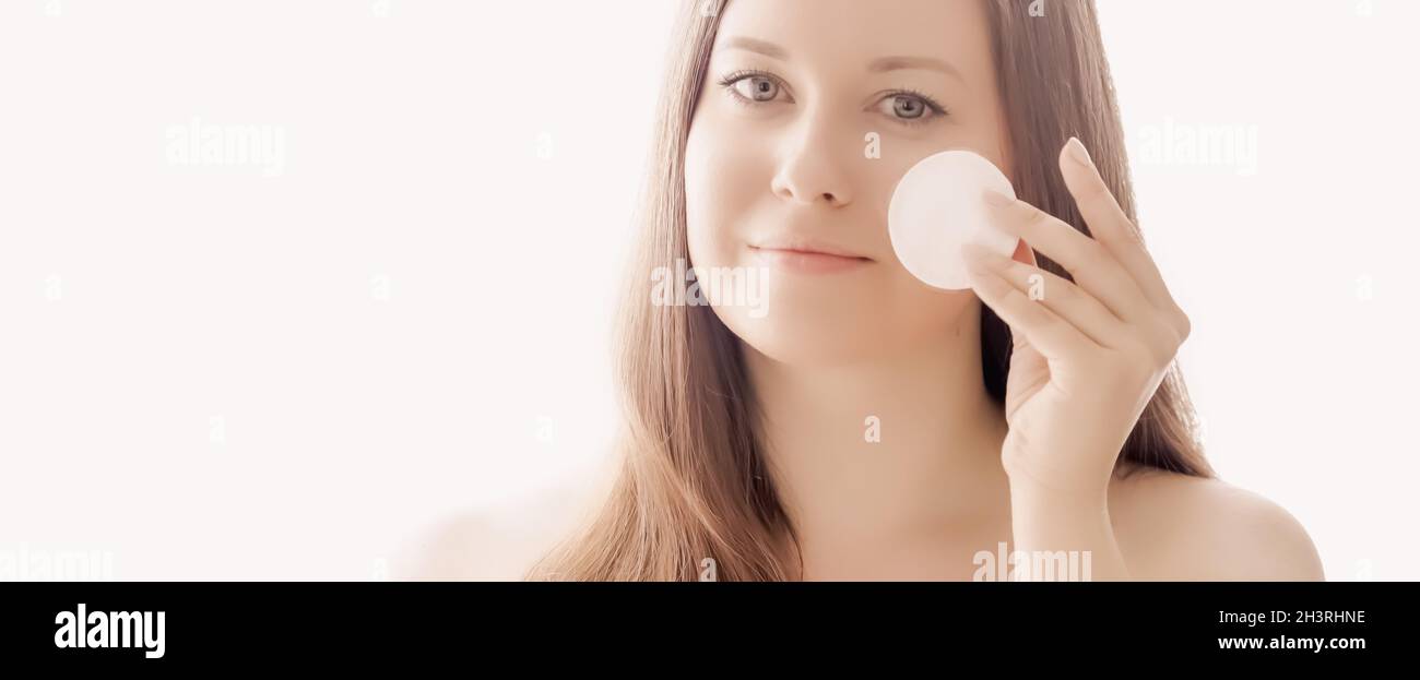 Beautiful woman with cotton pad, perfect skin and shiny hair as make-up ...