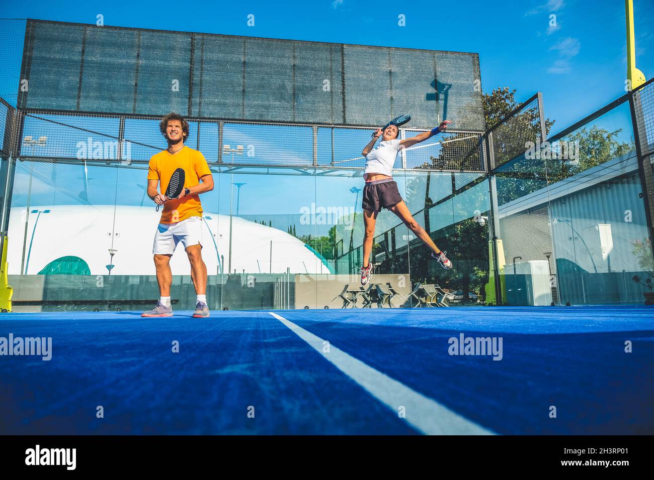Mixed padel match in a blue grass padel court - Beautiful girl and ...