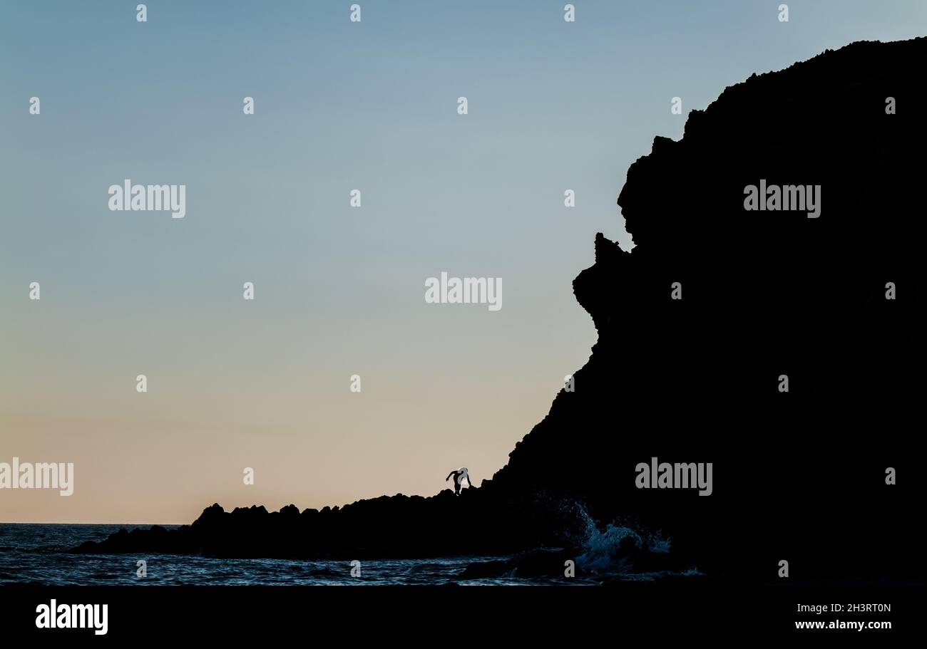 Silhouette of man climbing rock on beach during sunset Stock Photo - Alamy