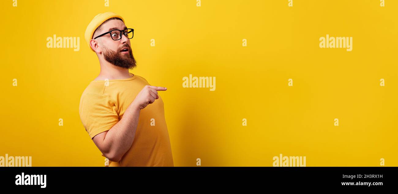 shocked man pointing on empty layout space over yellow background ...