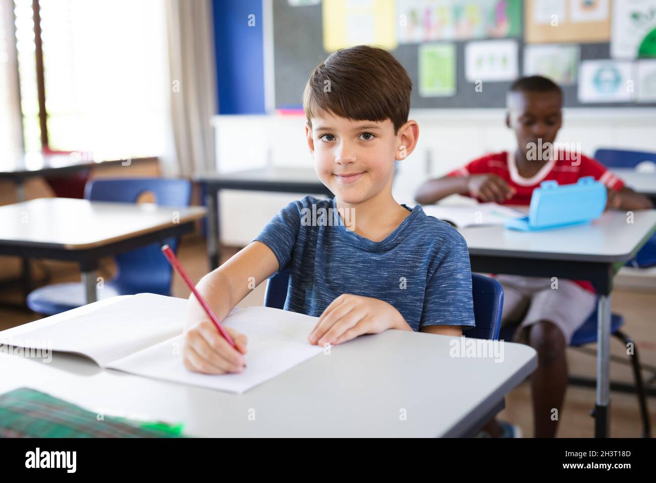 Portrait of caucasian boy smiling while sitting on his desk in the ...
