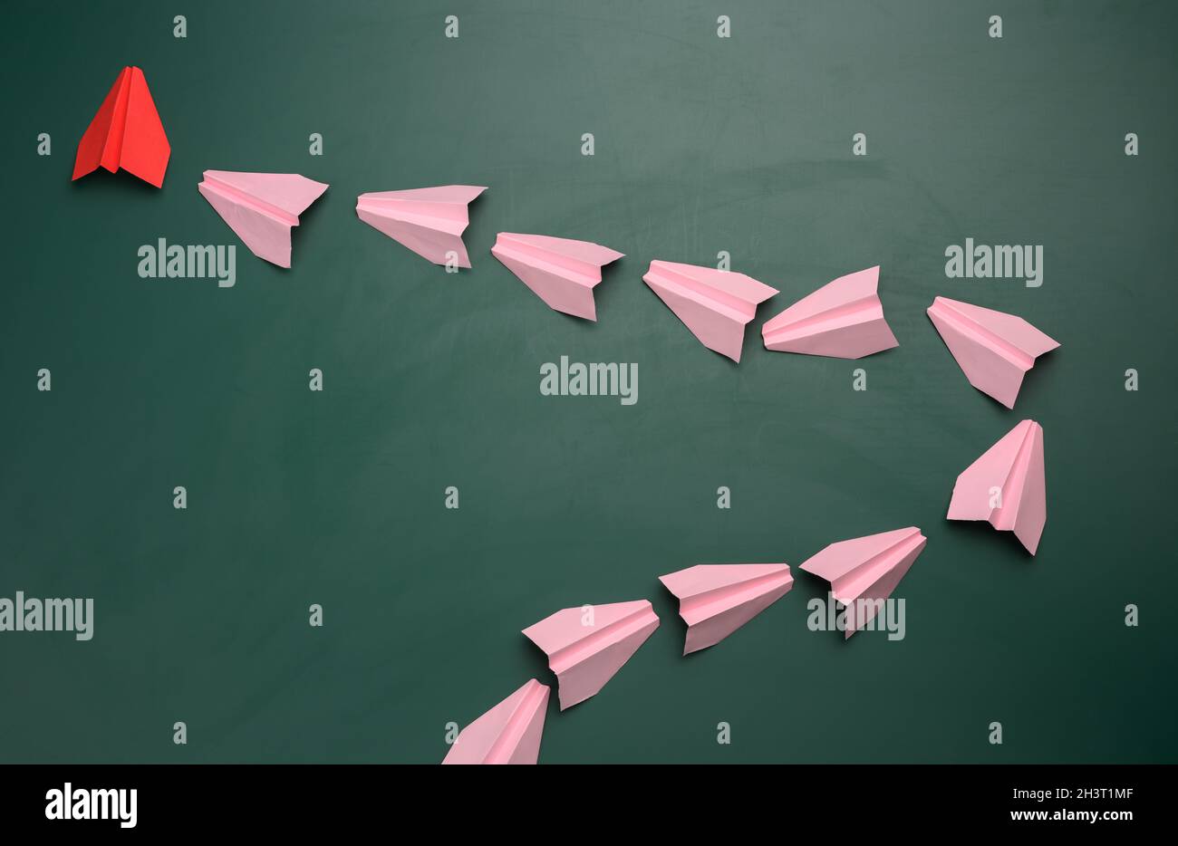 Group of pink paper airplanes following the first red on a green ...