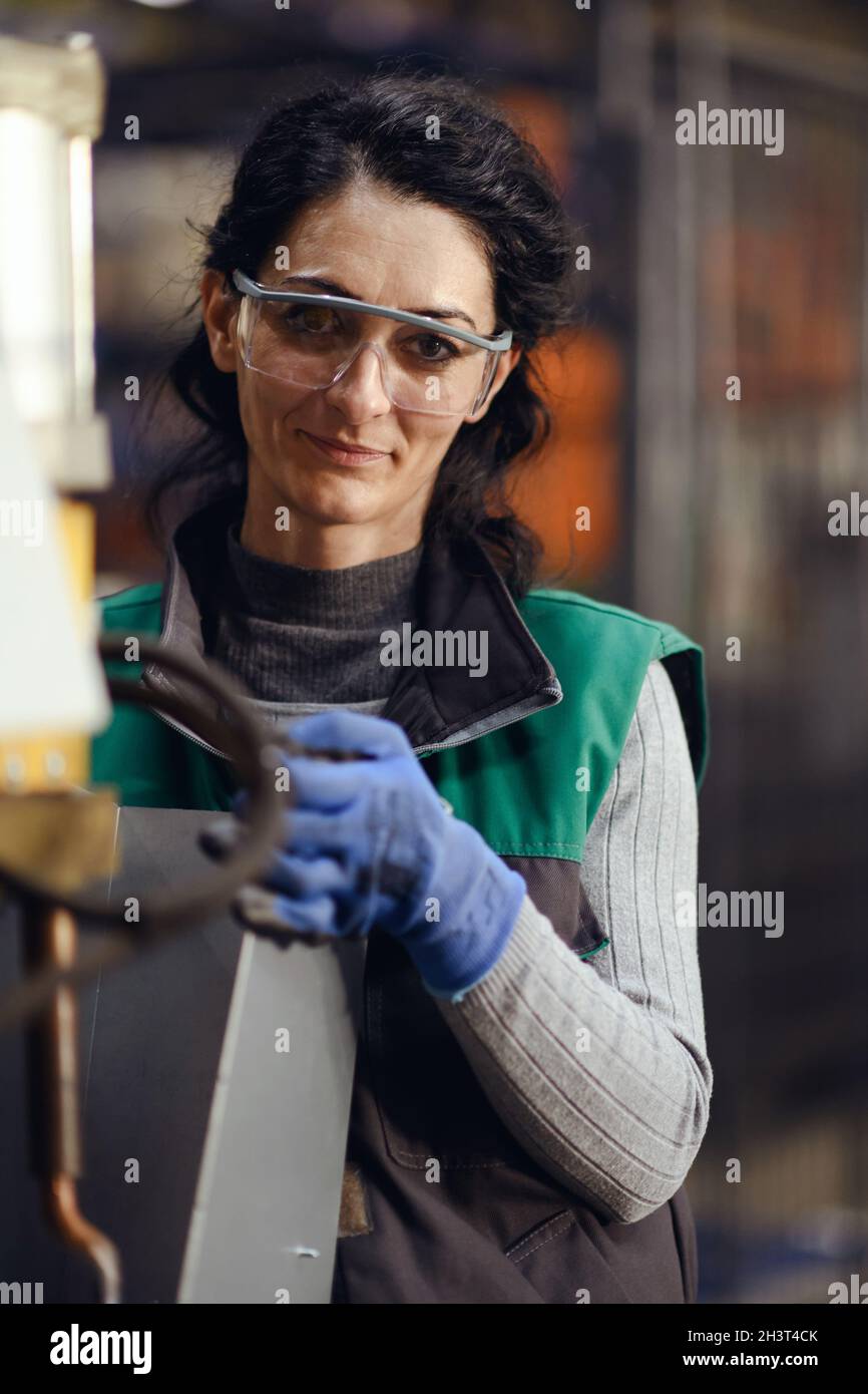 Woman worker wearing safety goggles control lathe machine to drill ...