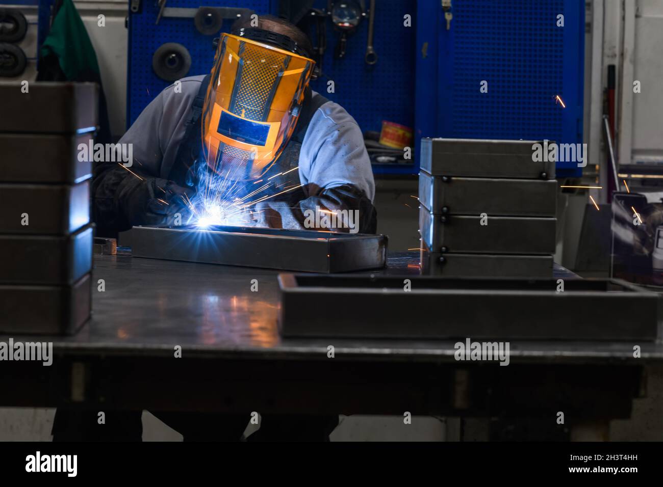 Professional welder performs work with metal parts in factory, sparks ...