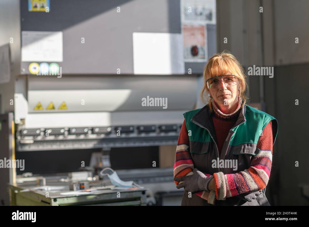 Portrait of a woman standing in front of a CNC machine in goggles and ...