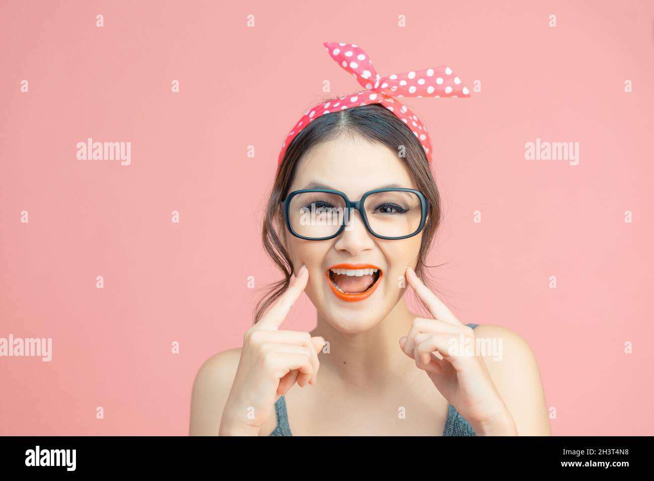 Image of happy asian woman smiling and pointing finger at her cheeks ...