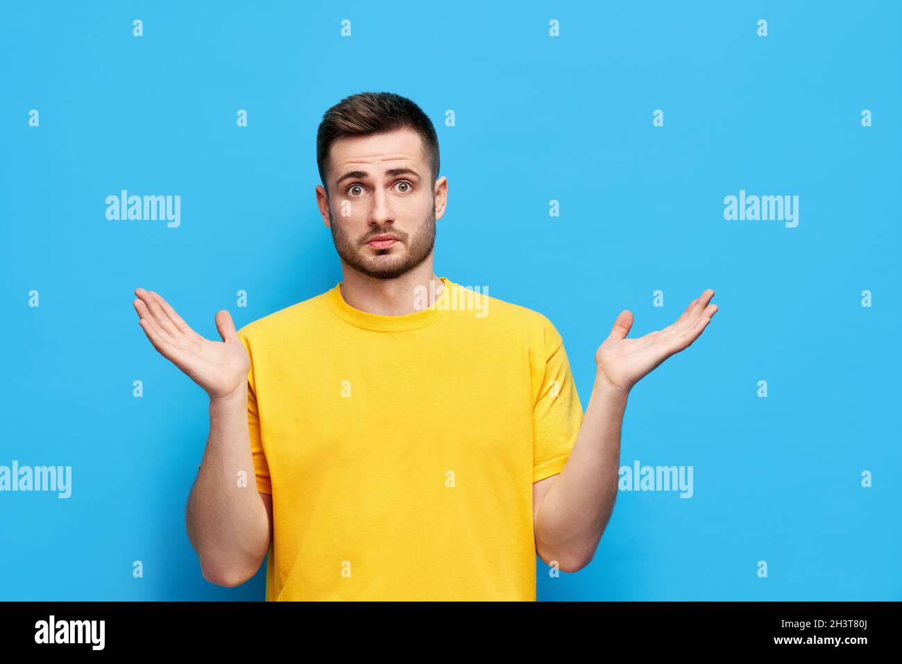 Young confused man spreads hands sideways feels doubt while makes ...