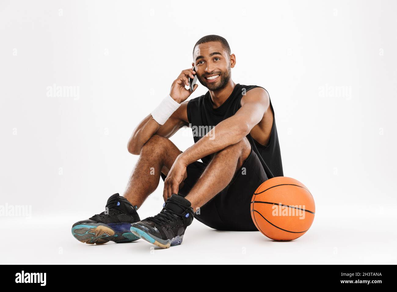 Happy african young basketball player sitting talking on mobile phone ...