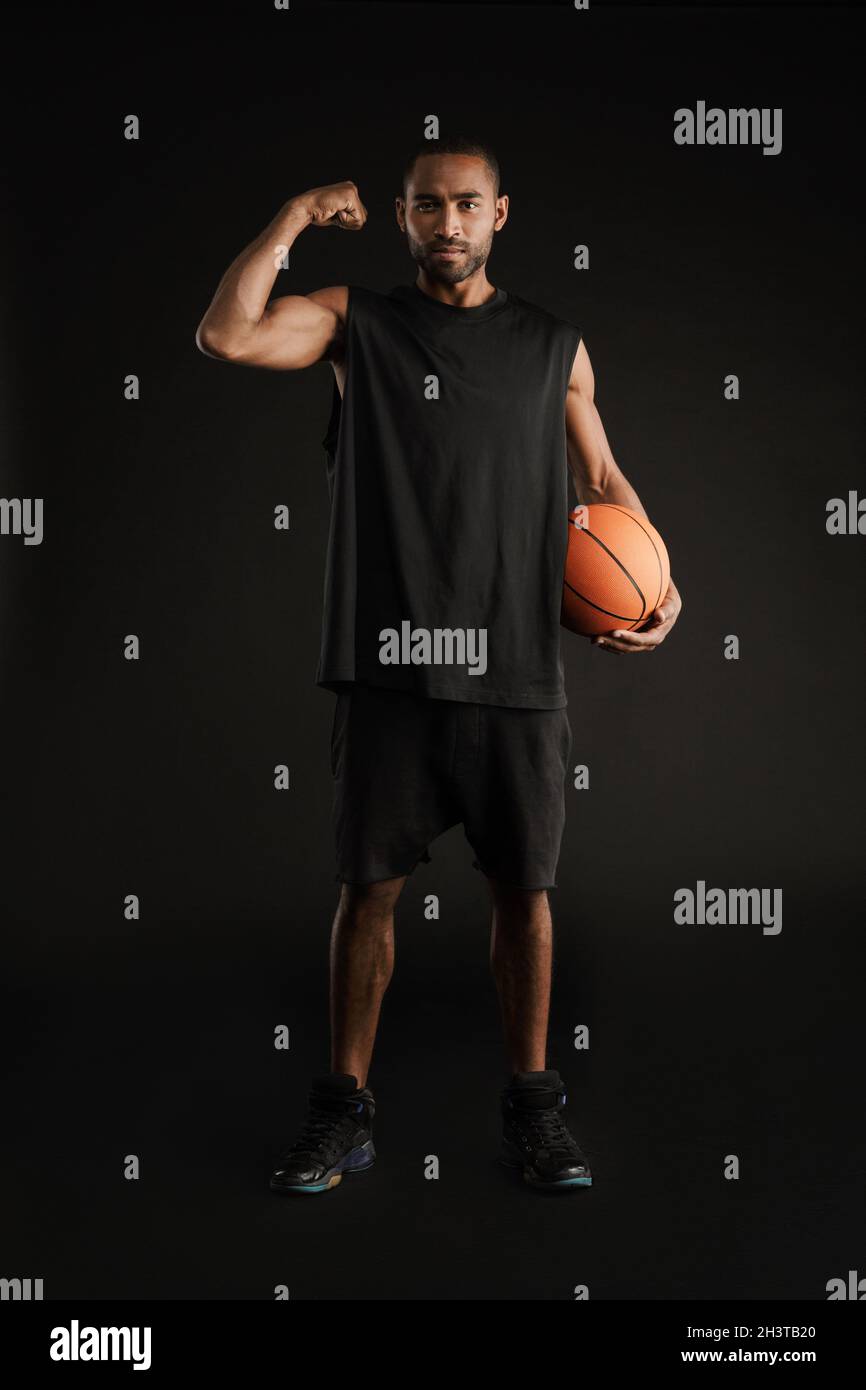 Young sportsman showing his bicep while posing with basketball isolated ...