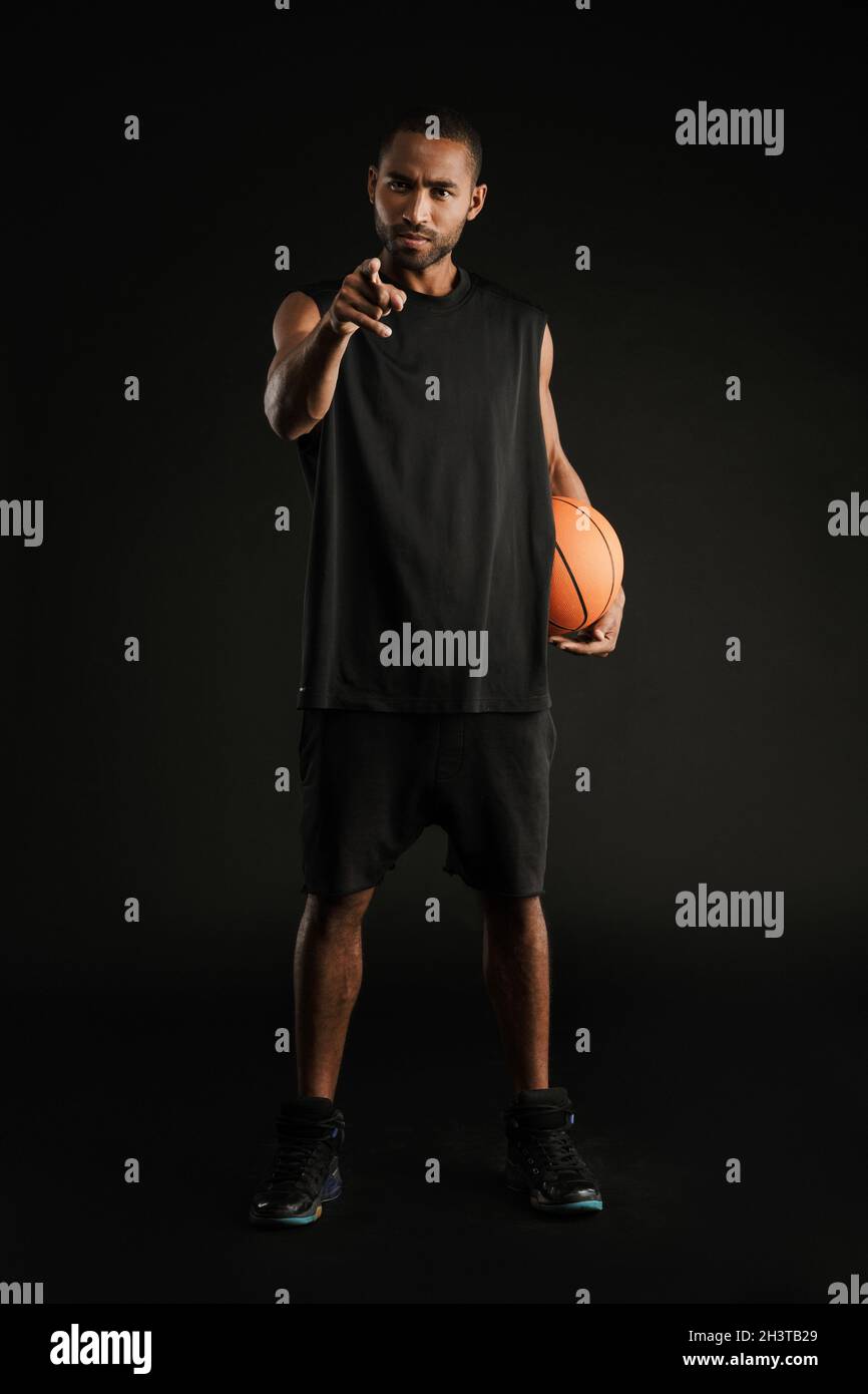 Young sportsman pointing finger at camera while posing with basketball ...