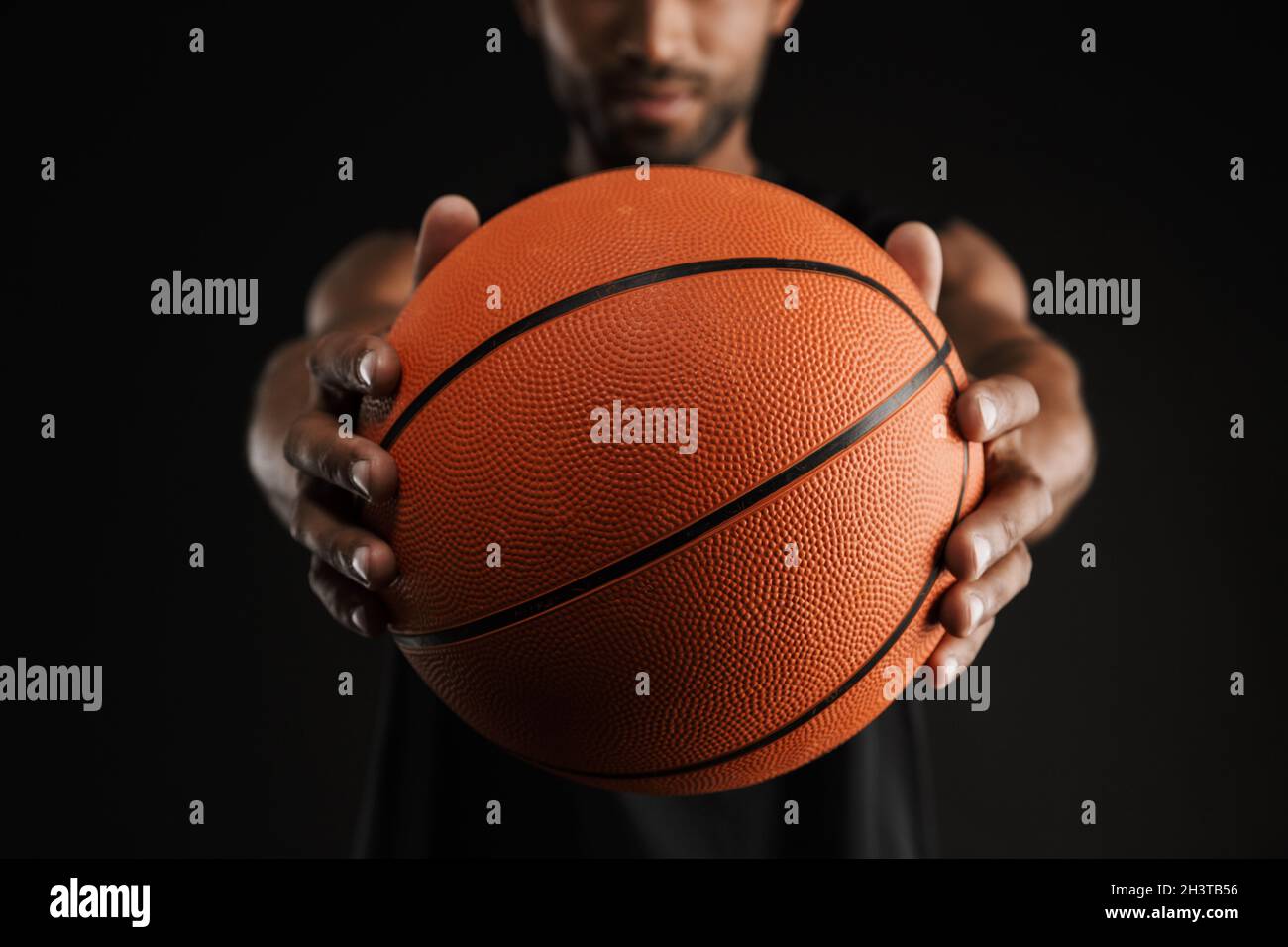 Young sportsman looking and reaching basketball at camera isolated over ...