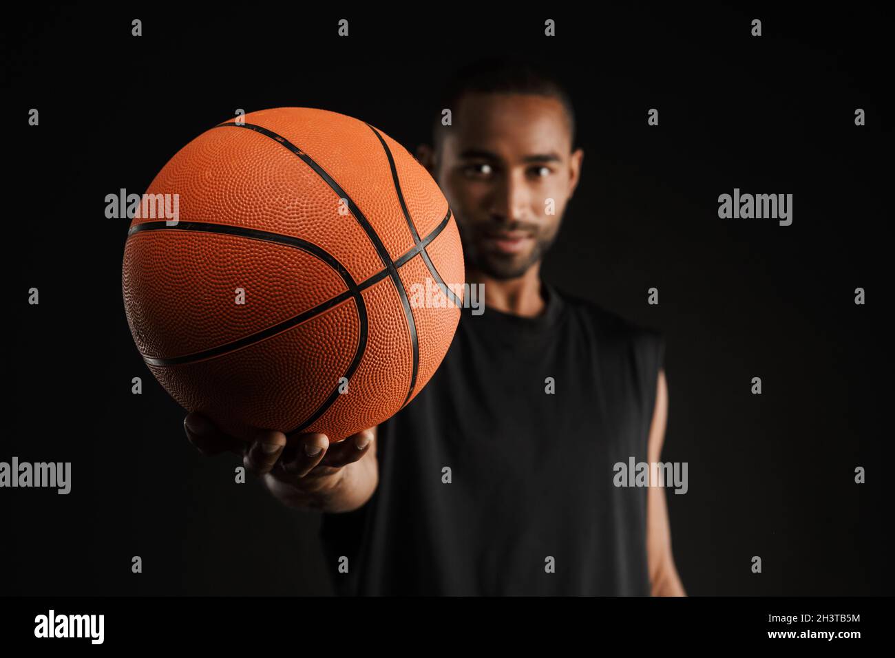 Young sportsman looking and reaching basketball at camera isolated over ...