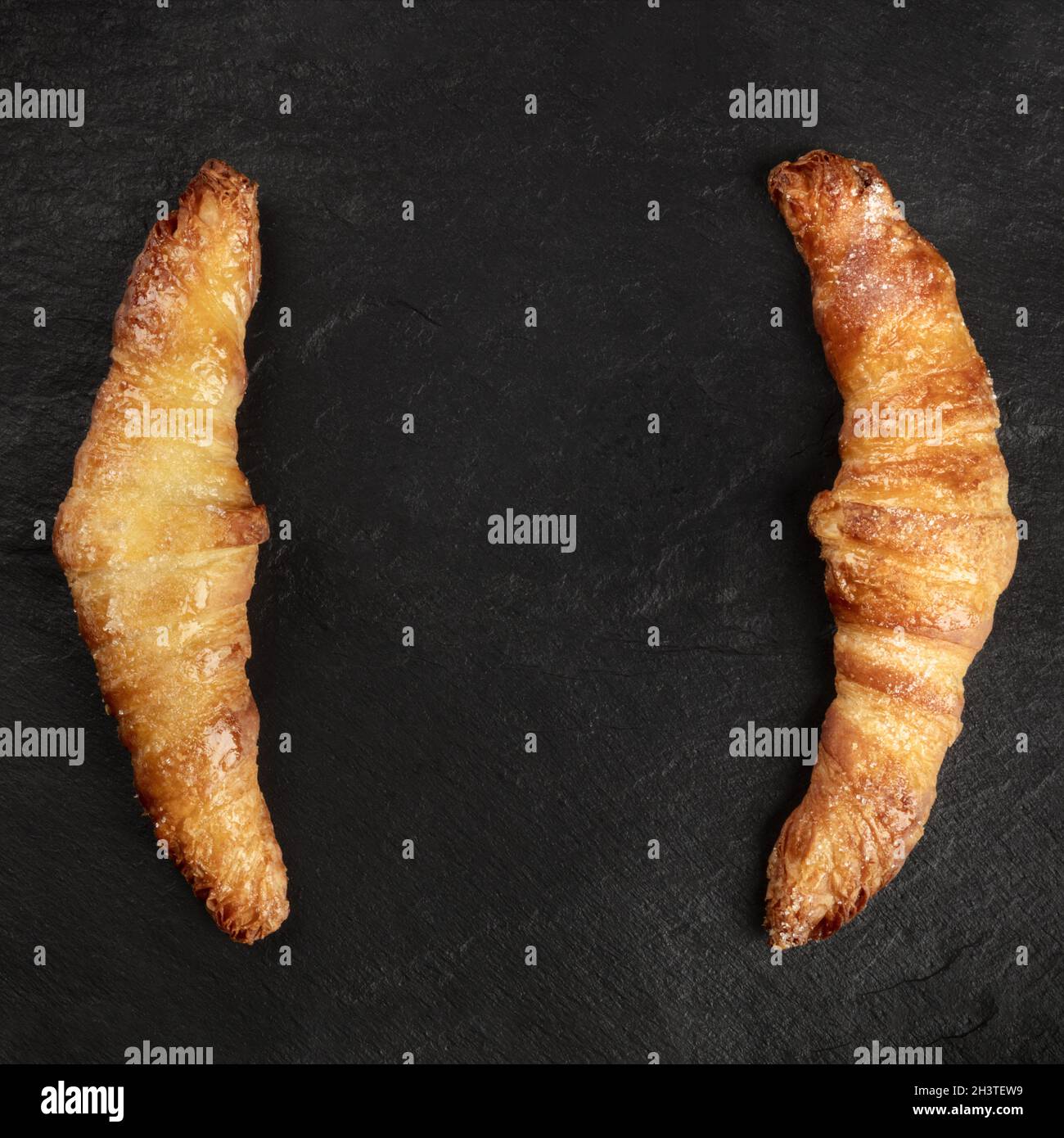 Two croissants on a black background, shot from the top, forming a ...