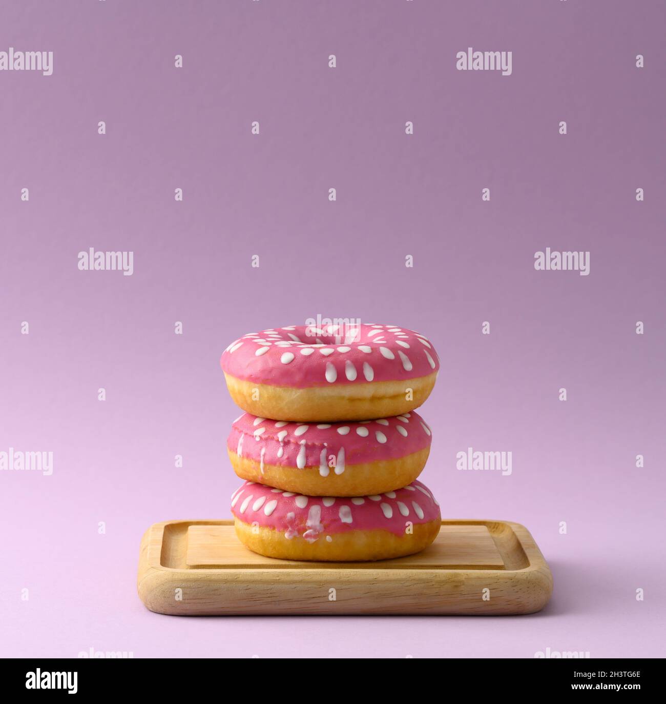 A stack of pink donuts with icing on a purple background Stock Photo ...