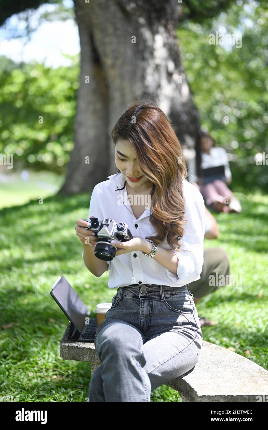 Young woman sitting on bench in the park and checking photos in camera ...
