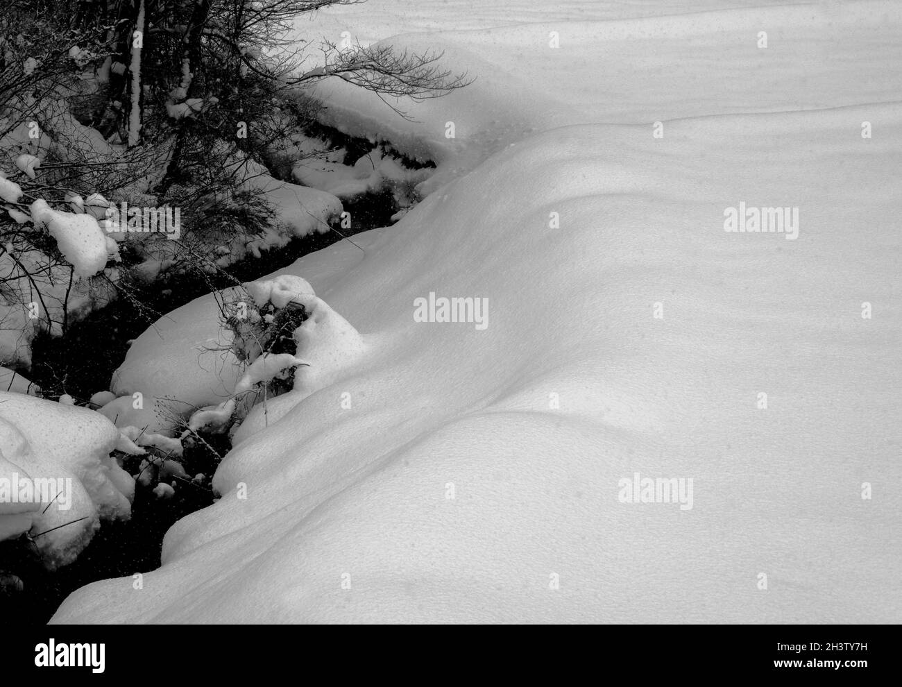 A winding drainage ditch at the bottom of snow-covered fields that ...
