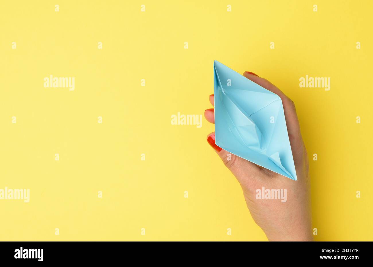 Female hand hold a blue paper boat on a yellow background Stock Photo ...