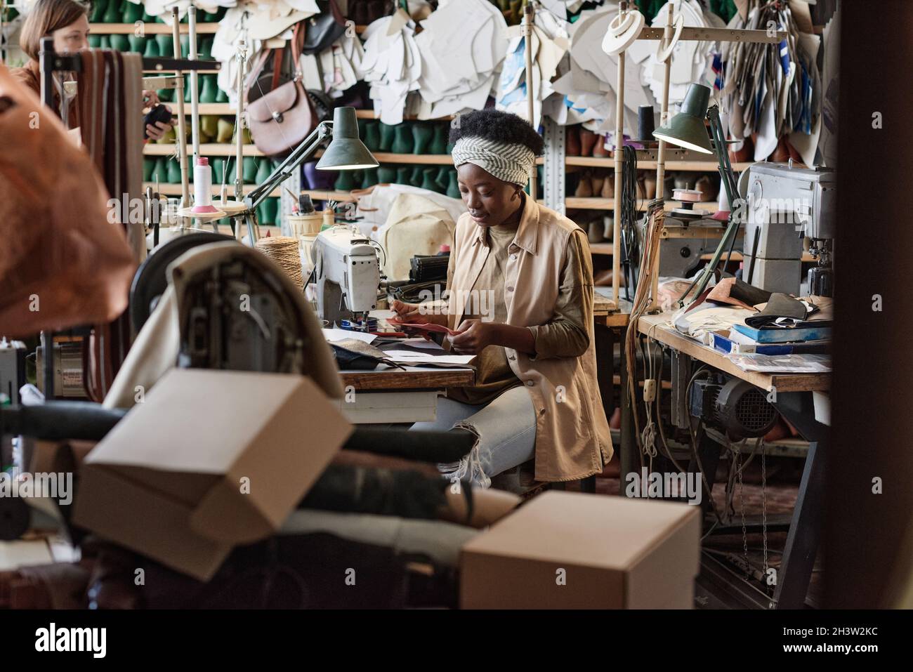 African dressmaker working at the table with fabric to sew new products ...