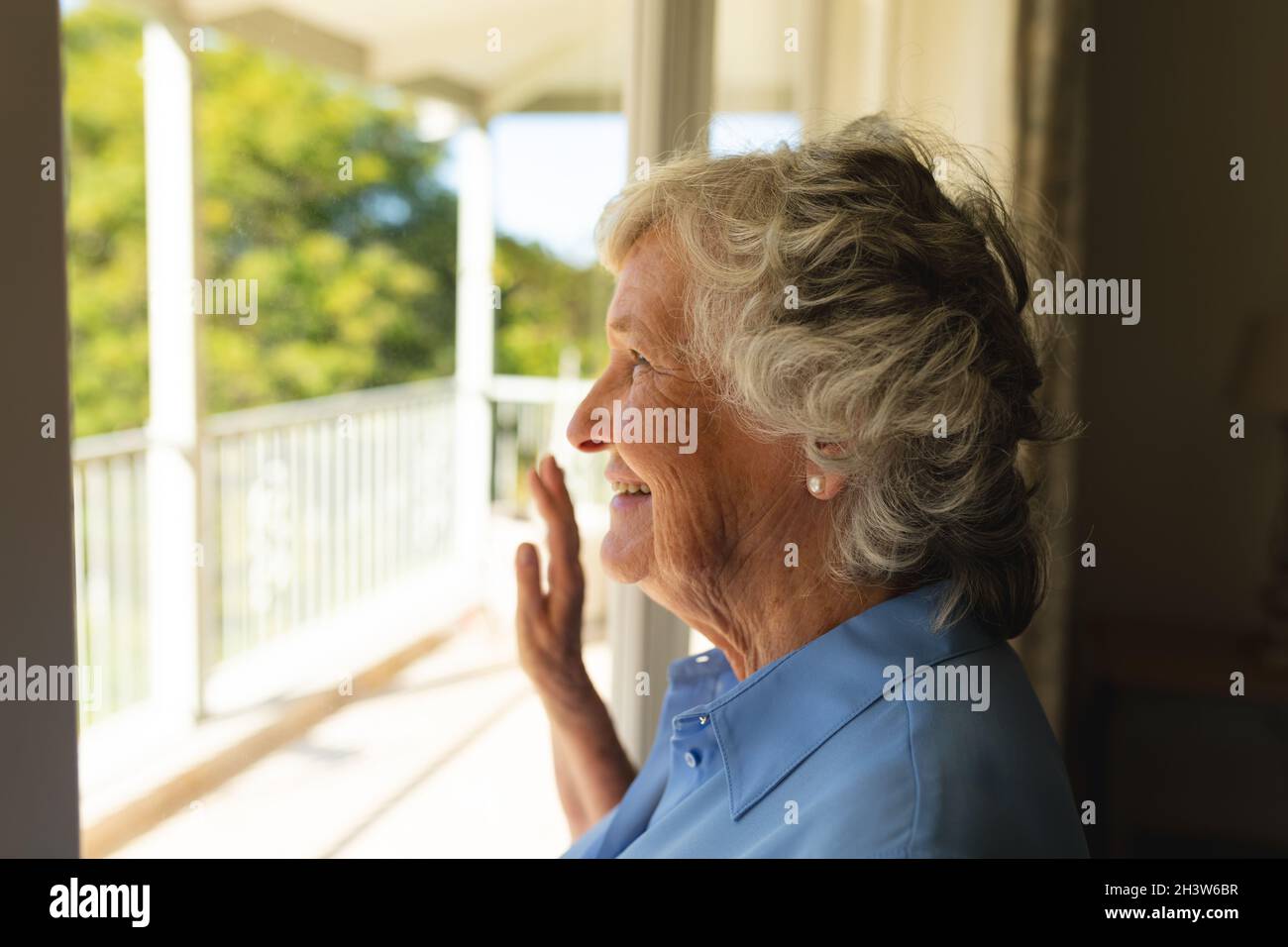 Senior caucasian woman looking through window and smiling Stock Photo ...