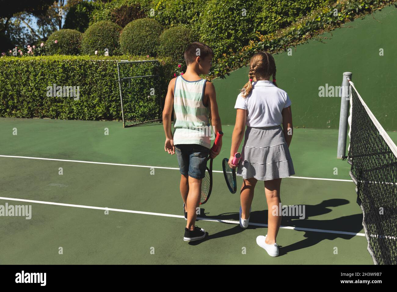Caucasian boy and girl outdoors, holding tennis rackets and walking on ...