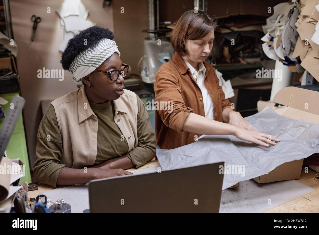 Two women sitting at the table and working in team, they packing boxes ...