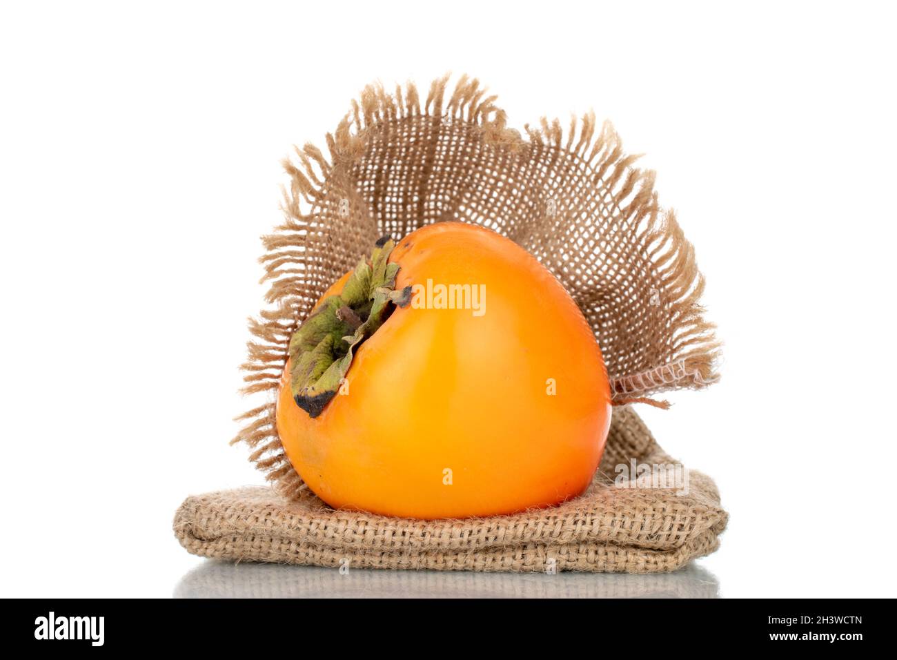 One organic persimmon with a bag of jute, close-up, isolated on white ...