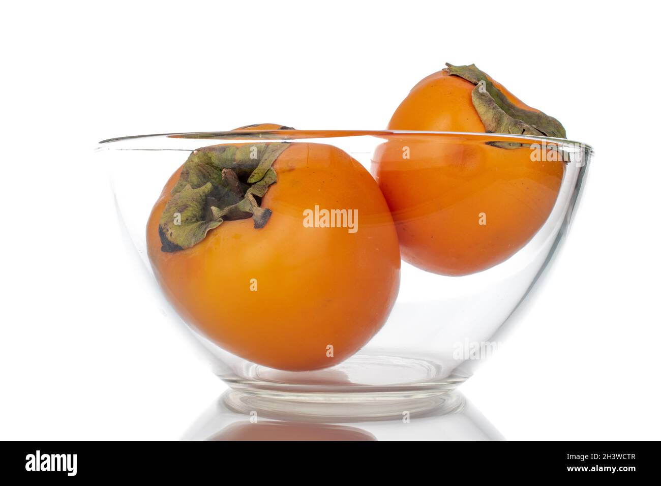 Two ripe sweet persimmons in a glass bowl, close-up, isolated on white ...