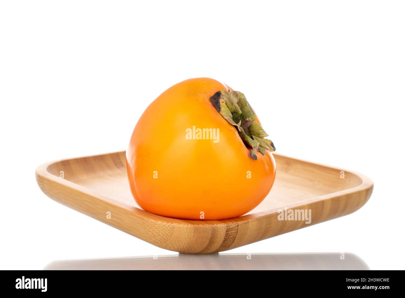 One organic persimmon on a bamboo plate, close-up, isolated on white ...