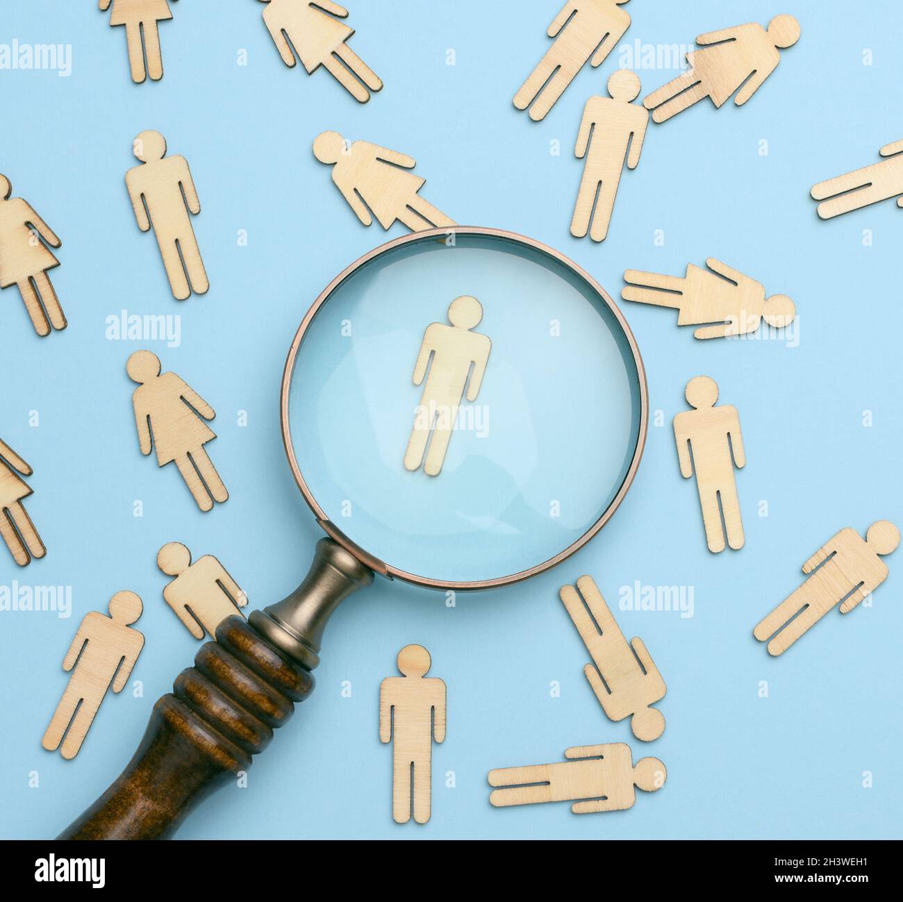 Wooden men and a magnifying glass on a blue background Stock Photo - Alamy