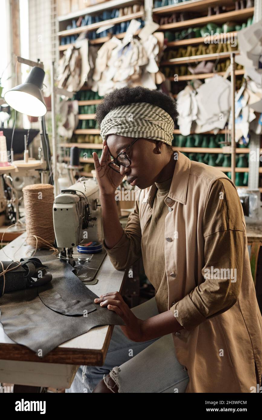 Tired tailor sitting at her workplace with sewing machine and holding ...