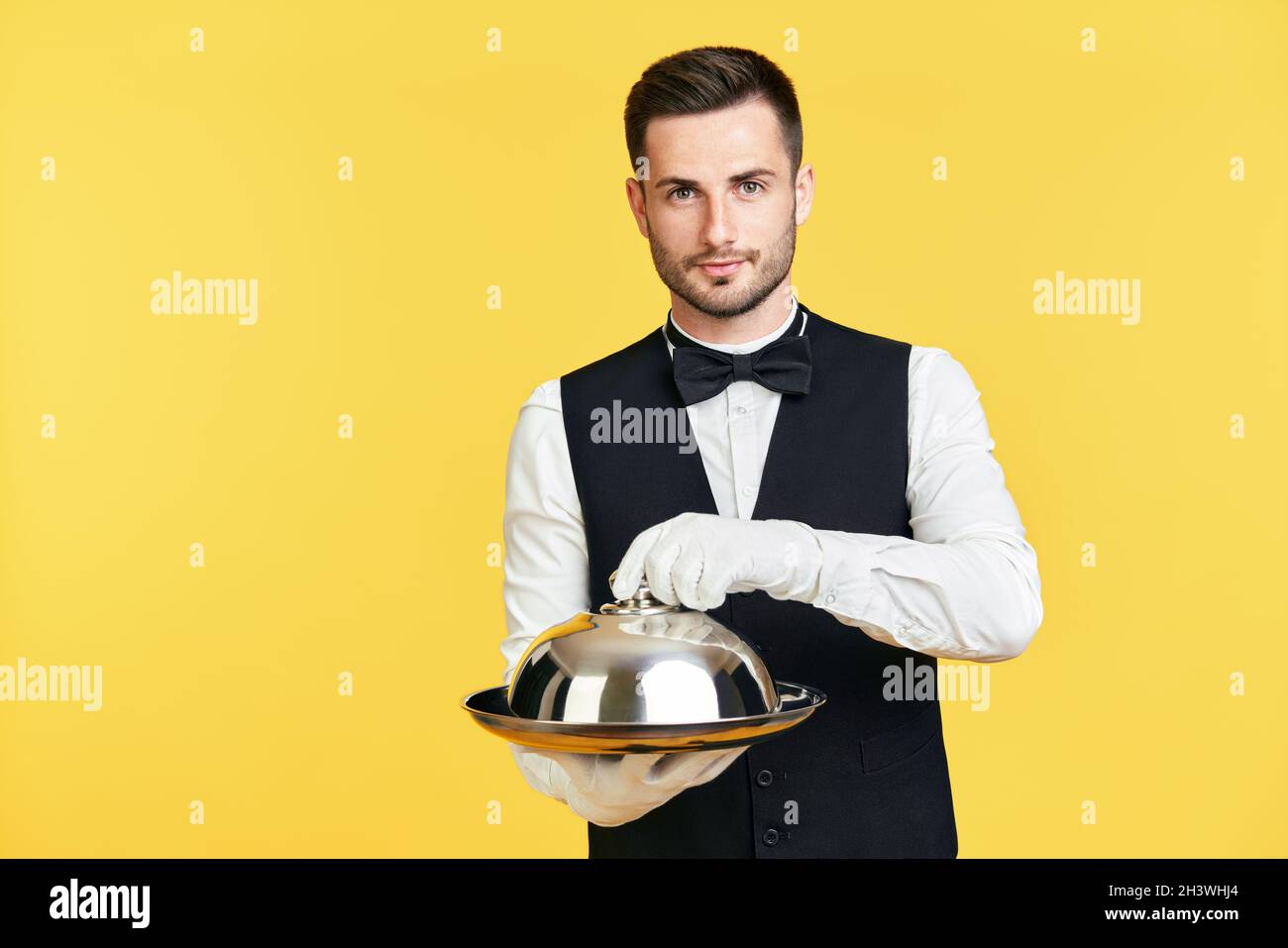 Young handsome waiter holding metal tray with cover ready to serve ...