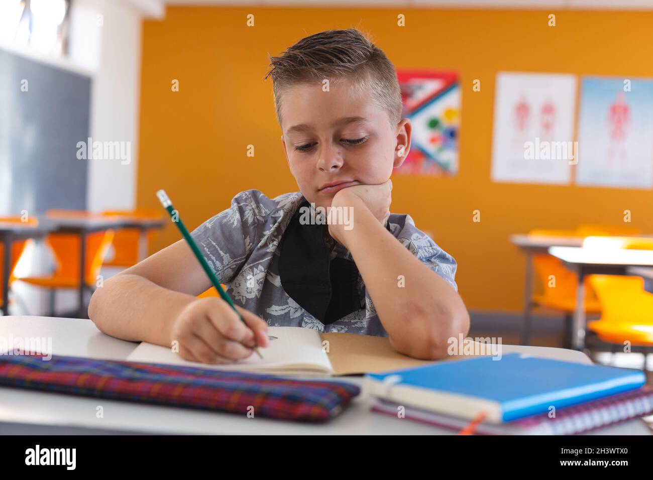 Caucasian schoolboy with face mask sitting in classroom concentrating ...