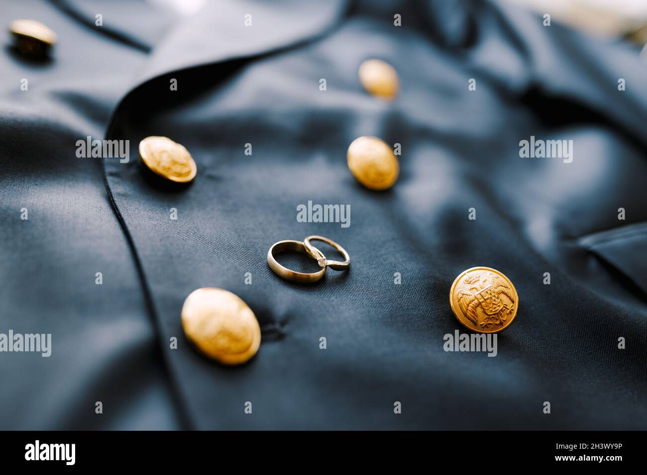 Two gold wedding rings on a blue men's jacket with buttons with a ...