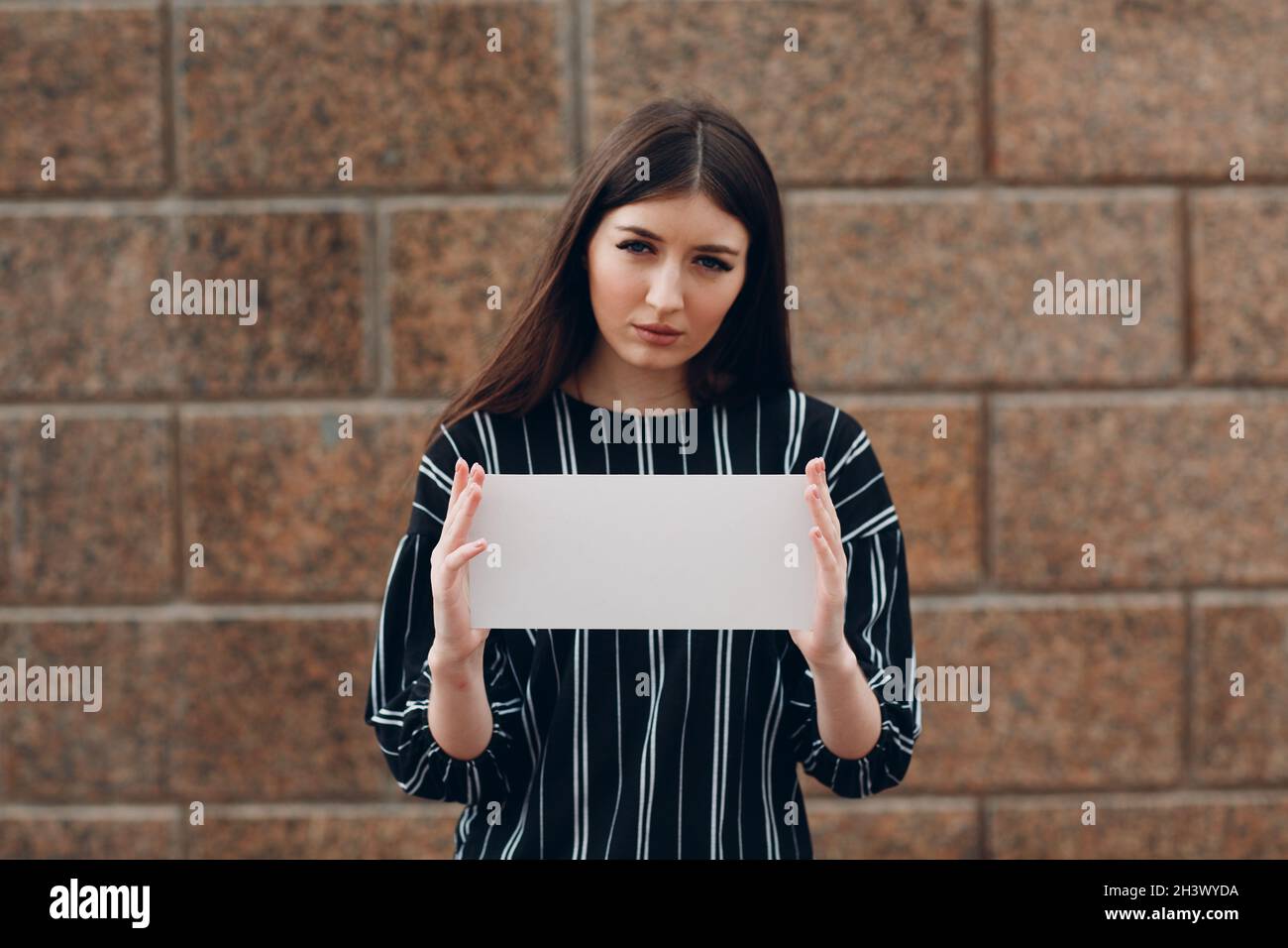 Sad girl holds white paper in hand stone background. Young woman with ...