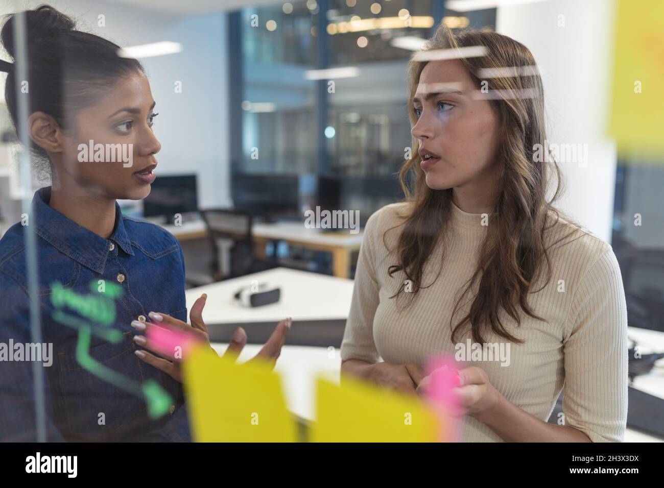 Two diverse female creative colleagues talking at meeting brainstorming ...