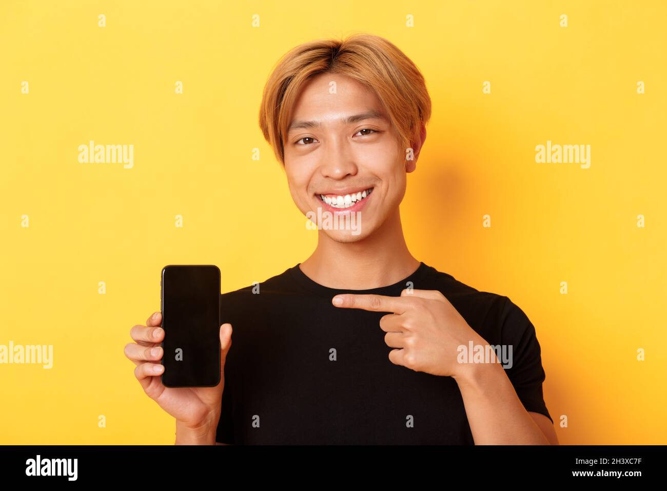 Cheerful attractive korean guy pointing finger at mobile phone screen ...