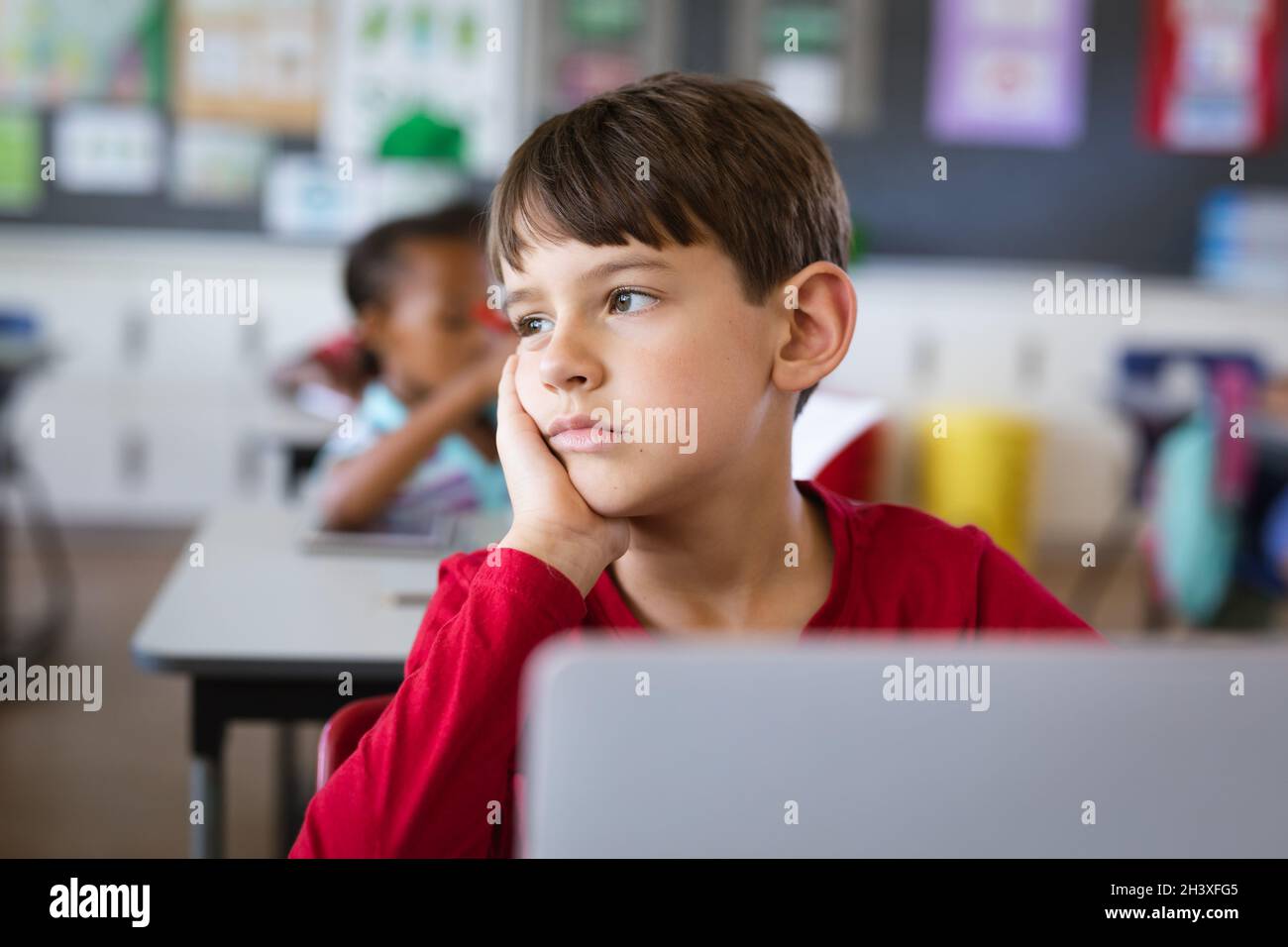 Sad caucasian boy with laptop sitting on his desk in the class at ...