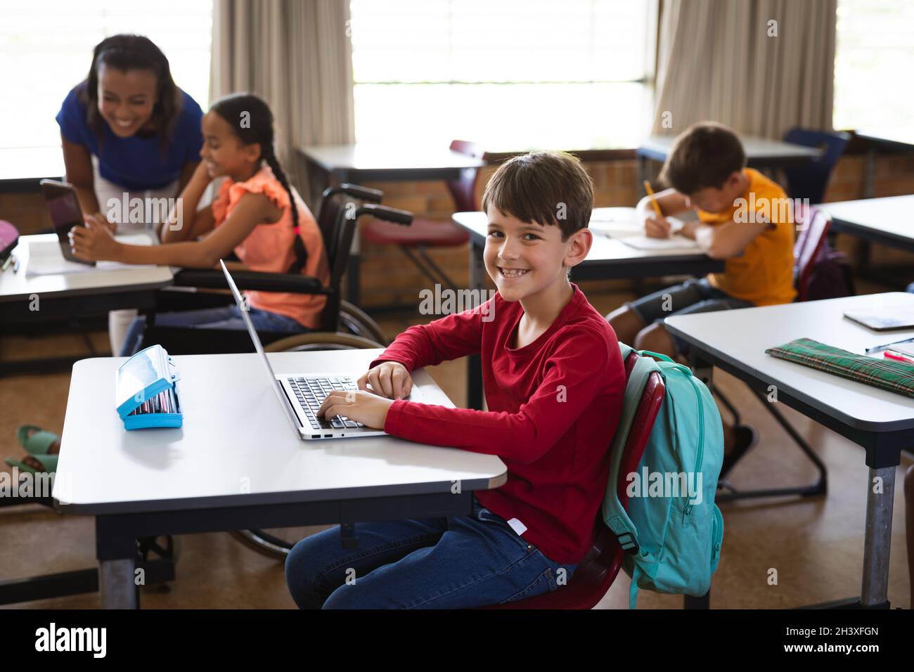 Portrait of caucasian boy with laptop smiling while sitting on his desk ...