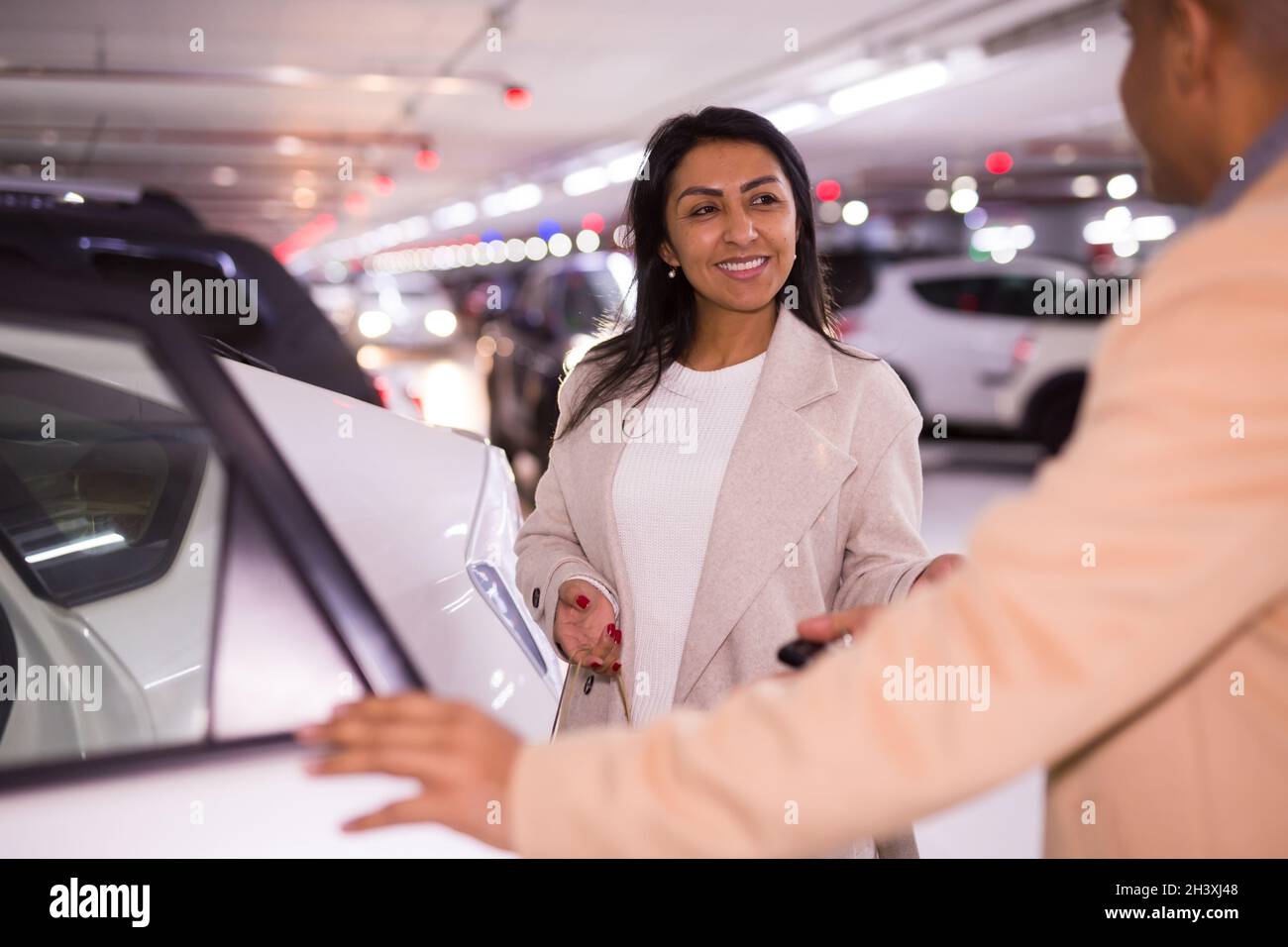 Smiling woman gets into a car in an underground parking lot. Man opens ...